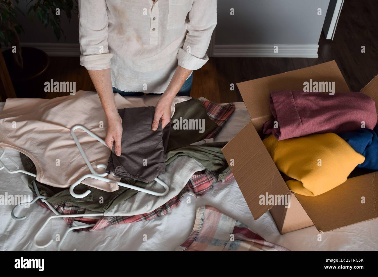 Woman is sorting through her clothes, folding and packing unwanted ...