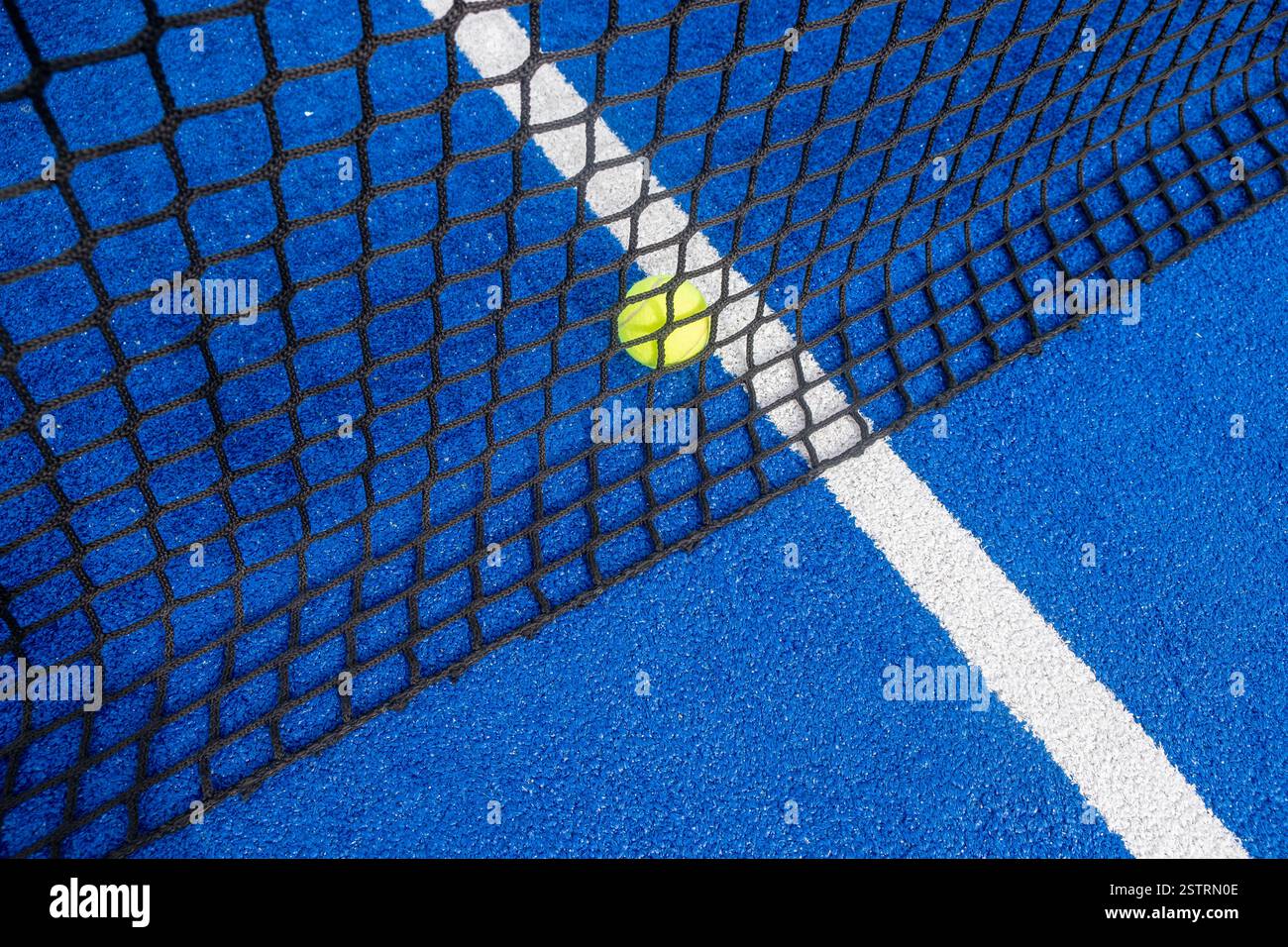 Tennis ball caught in a net on a vibrant blue court, highlighting the ...