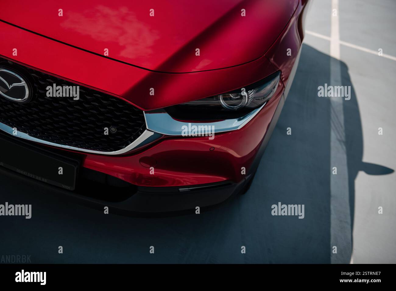 Front left corner of red Mazda CX-30 in hard afternoon light. close-up ...