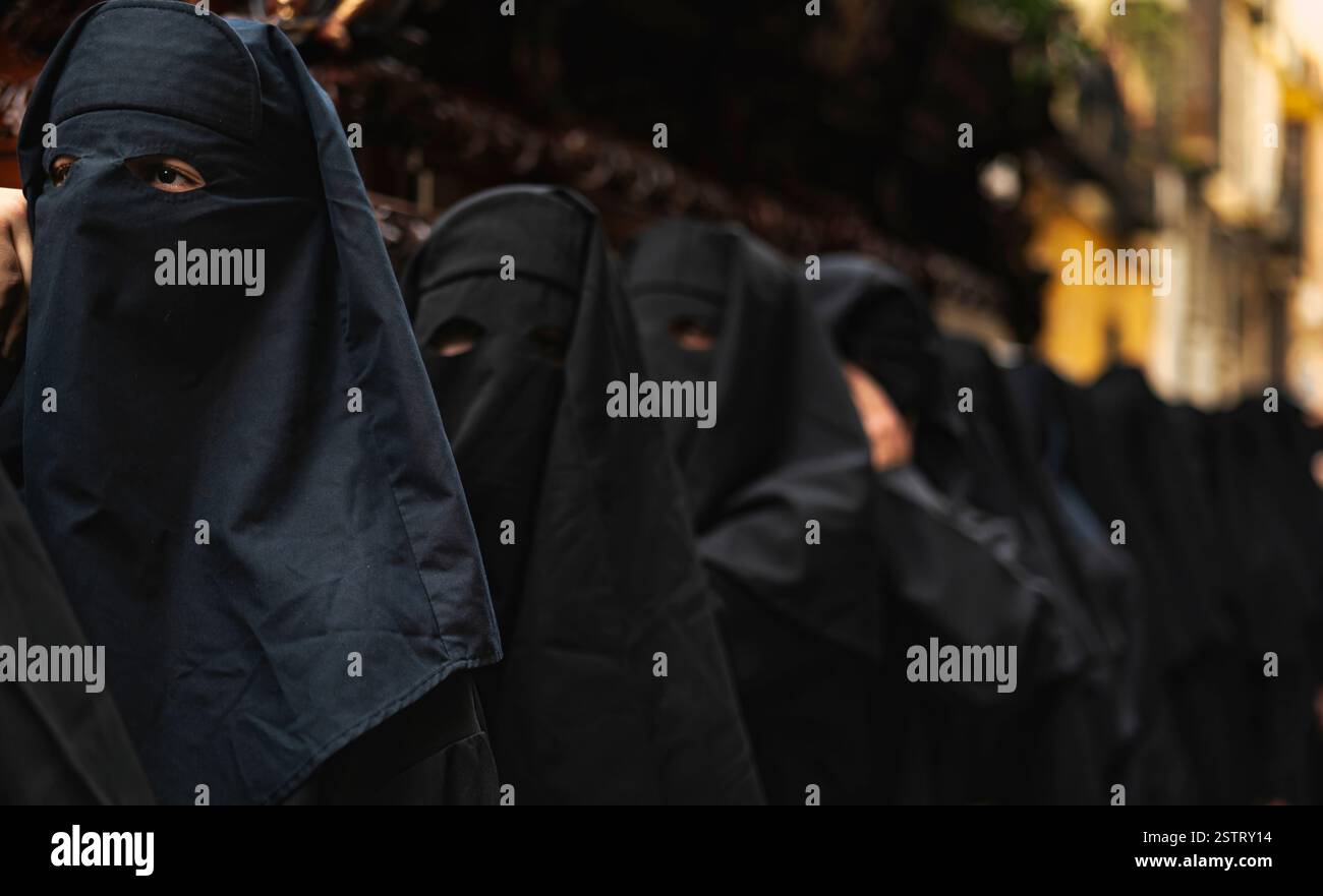Group of Nazarenes with black hoods advancing in line while carrying an ...