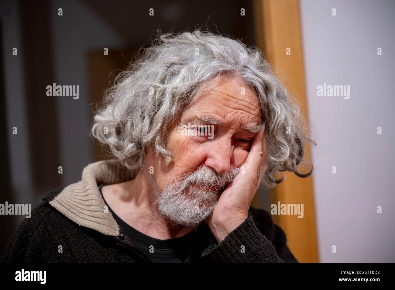 An elderly man with curly gray hair and a beard rests his head on his ...