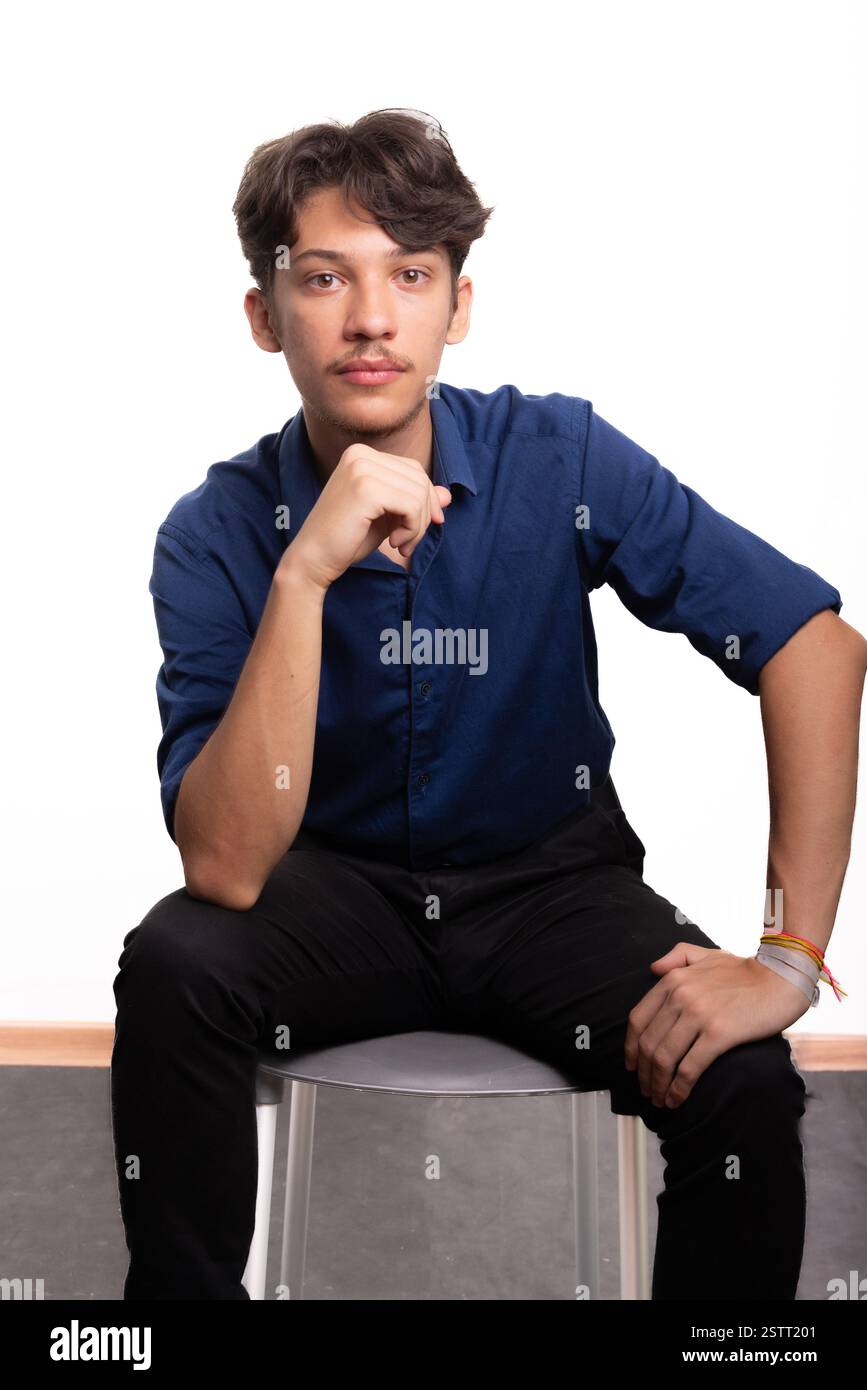 Young handsome student with black hair and blue shirt, sitting, looking ...