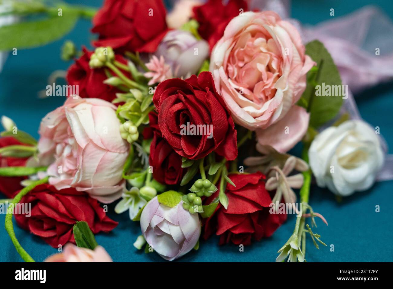 A vibrant arrangement of artificial flowers rests on a teal fabric ...