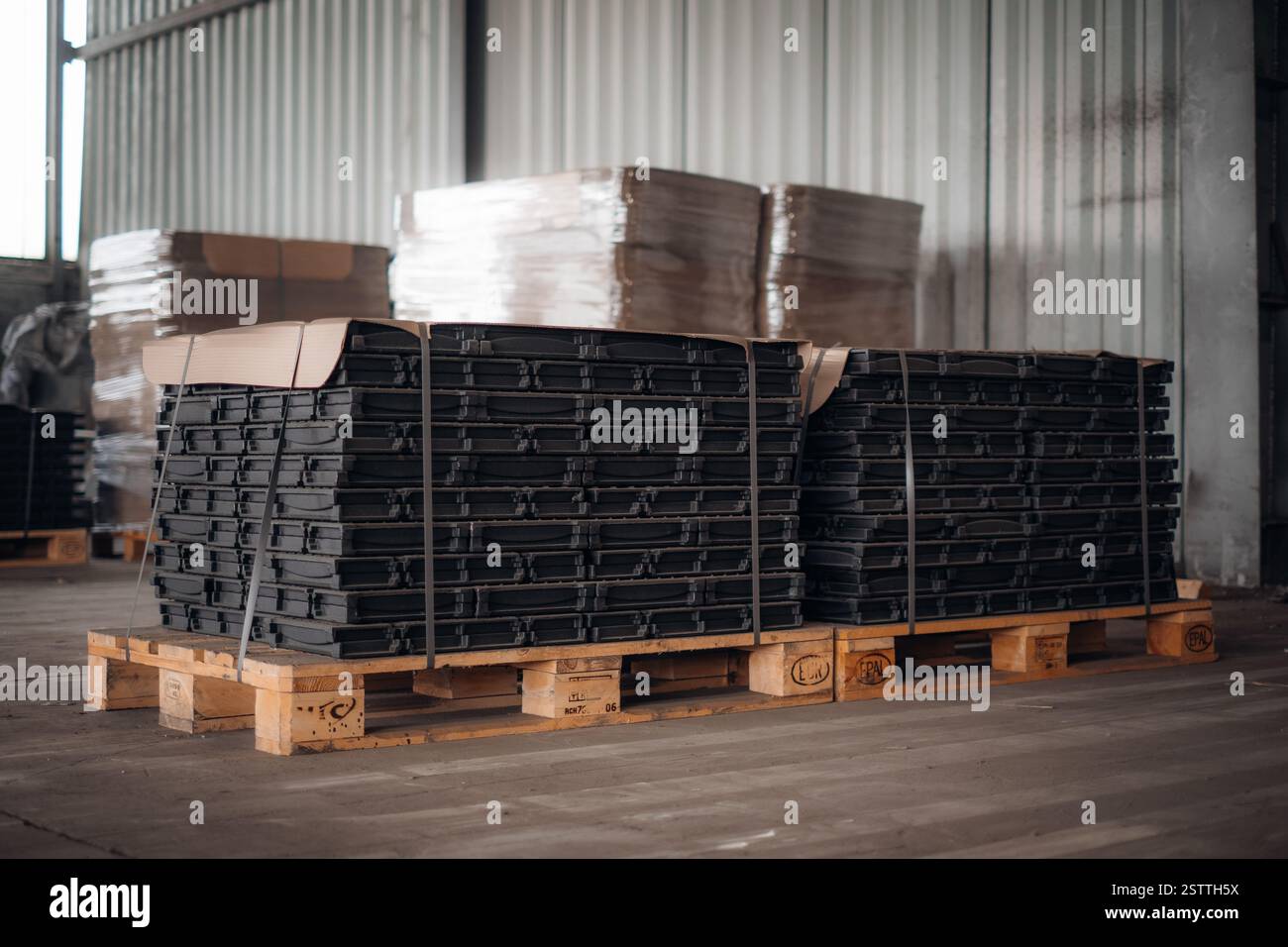 Stacks of black plastic components secured on wooden pallets in a ...