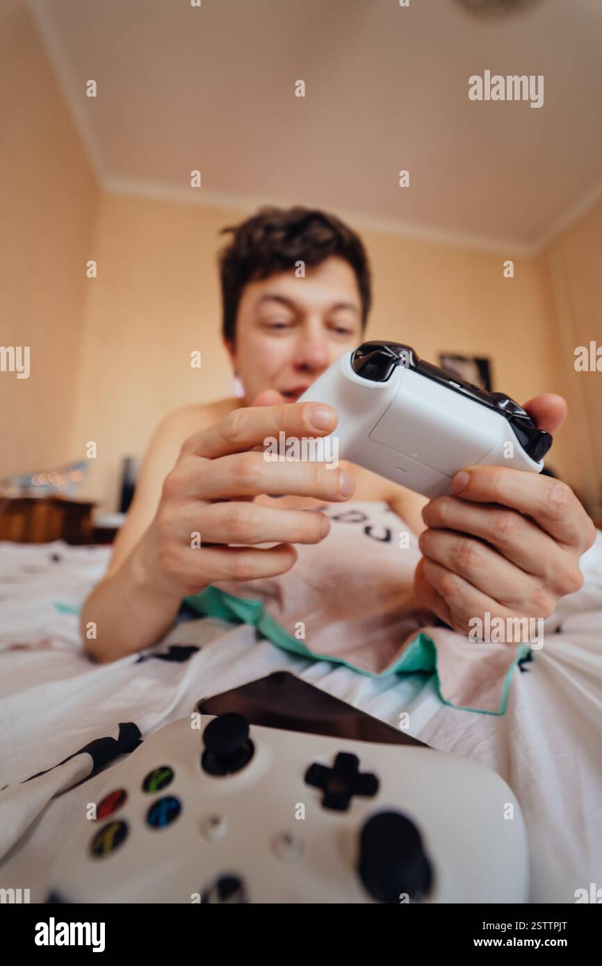 Guy lying in bed and playing video game, holding controller Stock Photo ...