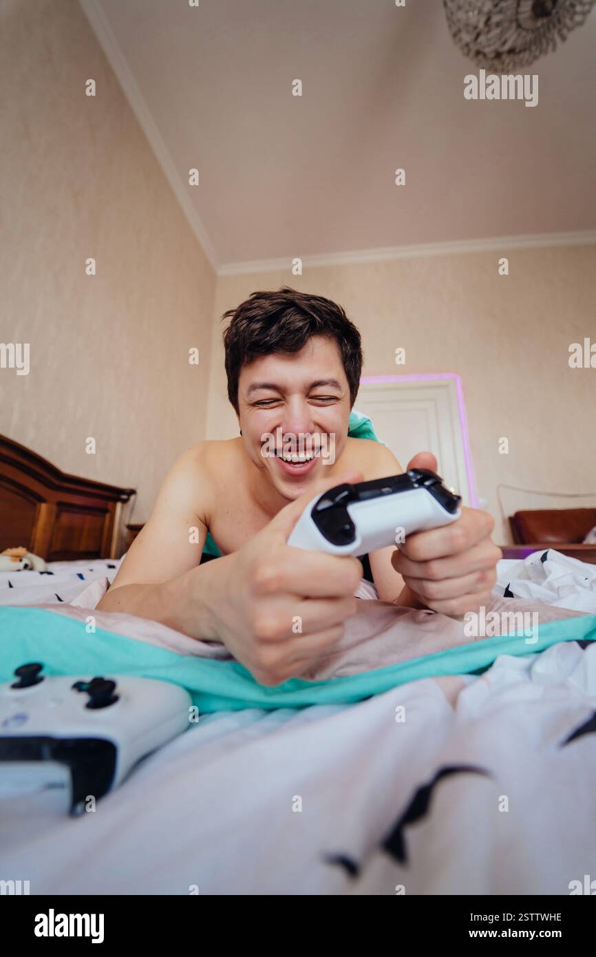 Guy lying in bed and playing video game, holding controller Stock Photo ...