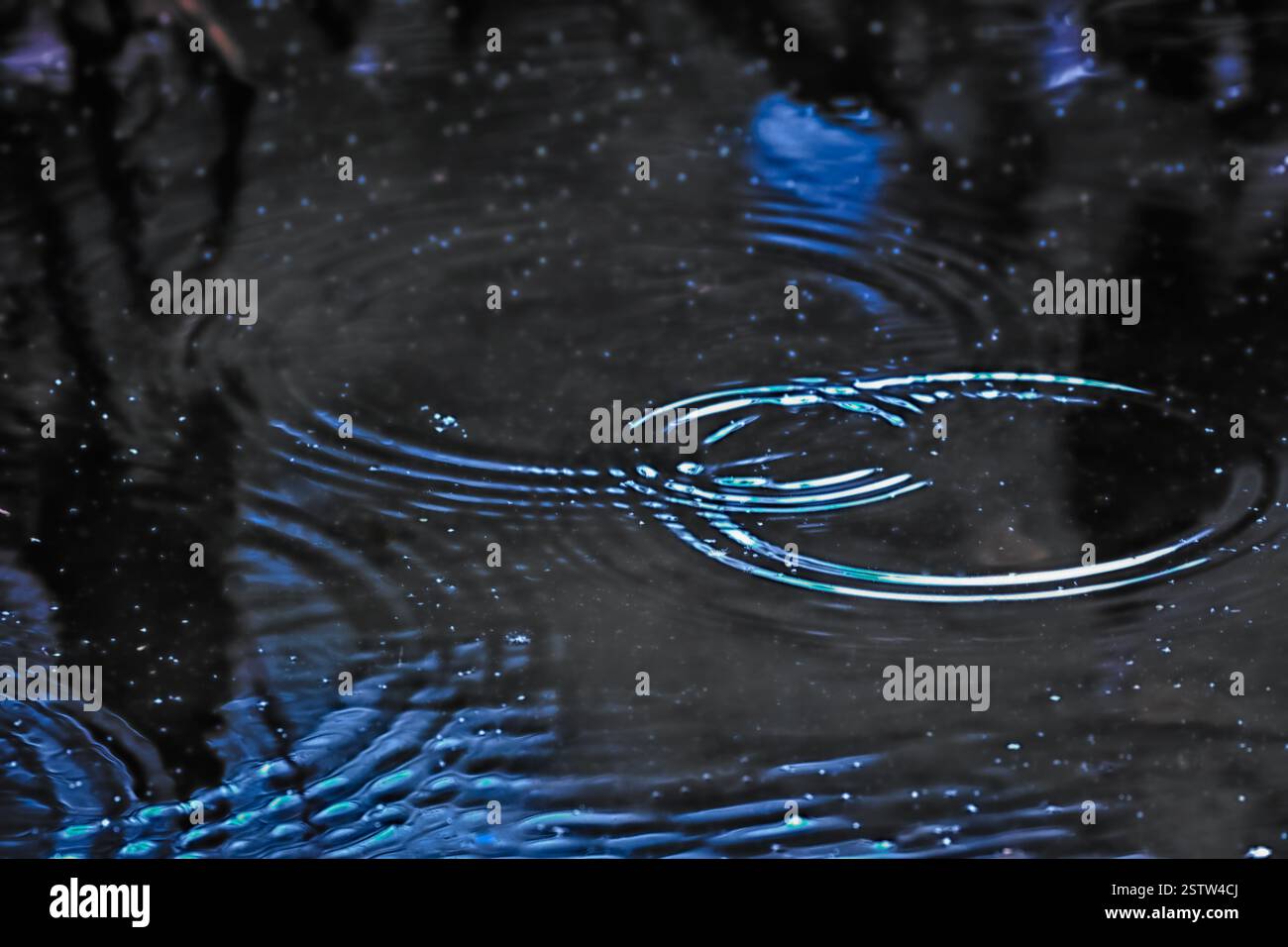 Close-up of ripples on a dark water surface with blue highlights, creating abstract reflections ...