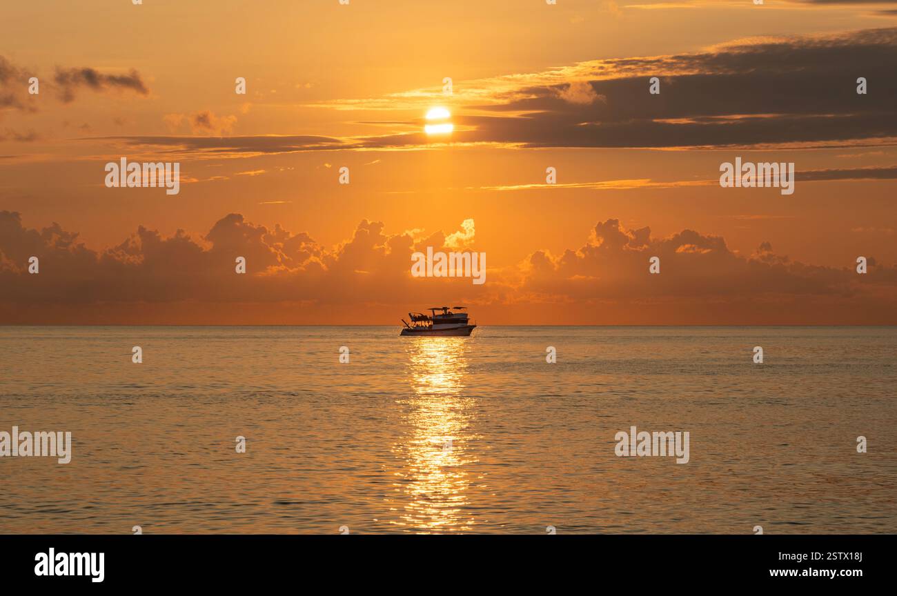 A boat glides across tranquil waters at sunset, with the sun’s golden ...