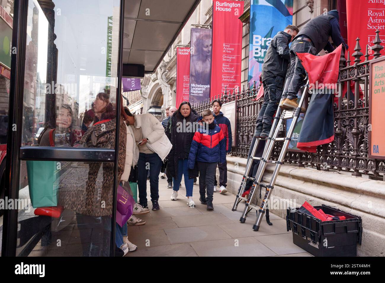 Workmen are up ladders in order to replace vertical banners that ...