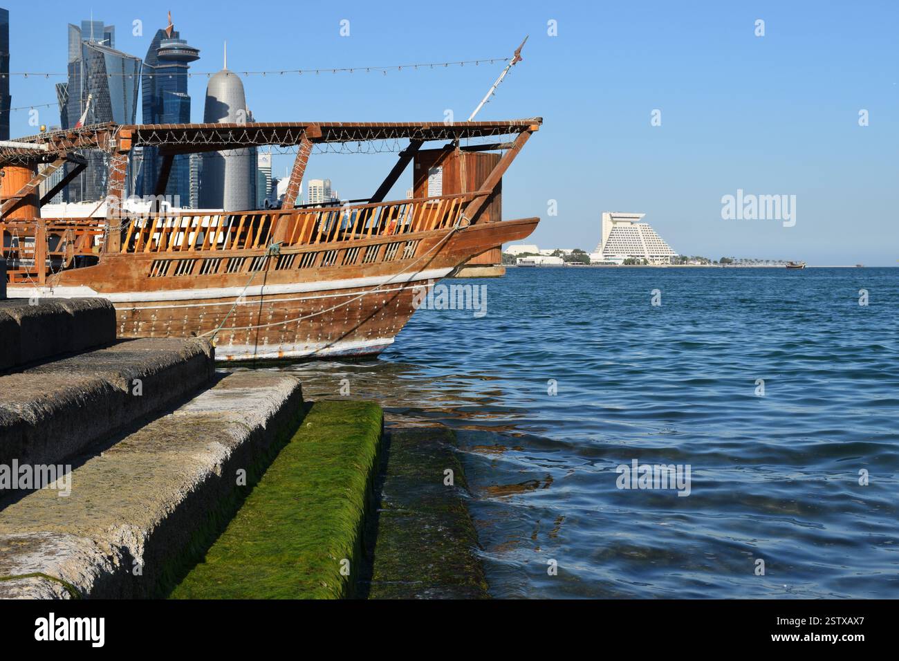 Traditional wooden dhow boat moored along Doha's Corniche with the city ...