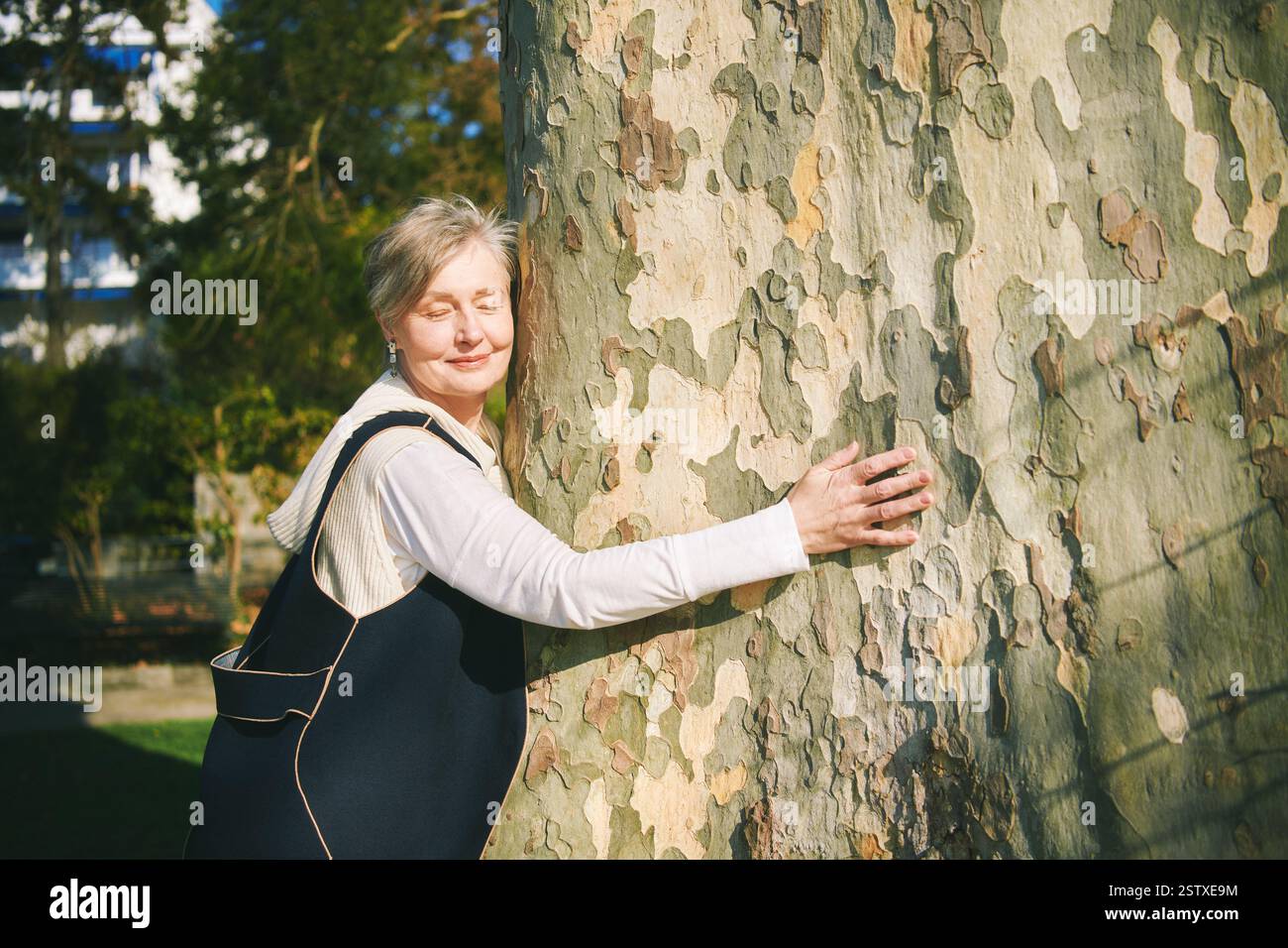 Outdoor portrait of happy middle age woman hugging the tree, connecting ...