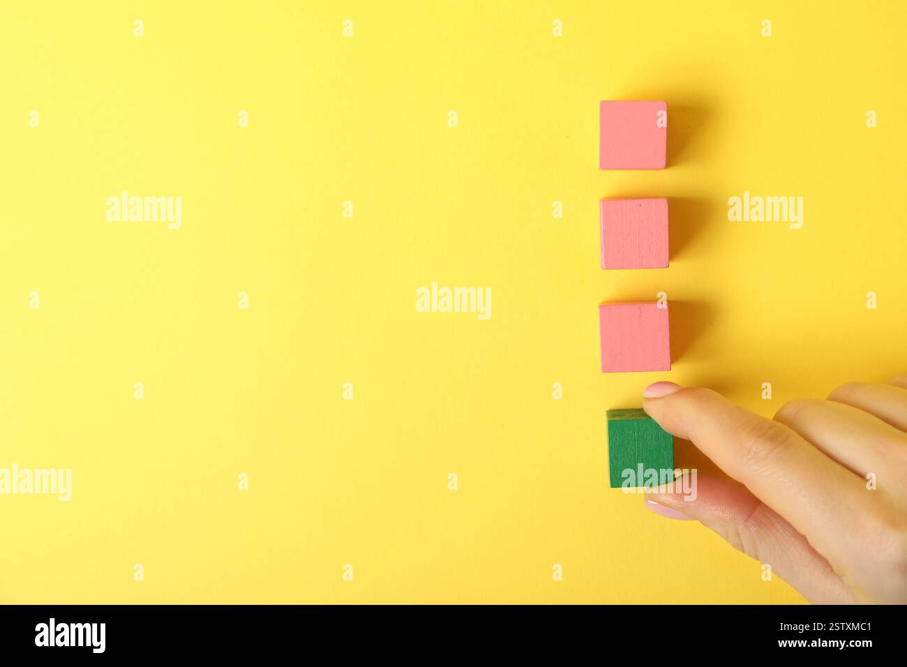 Woman taking green cube on yellow background, top view. Space for text ...