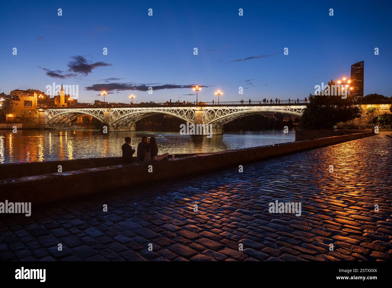 The Triana Bridge (Puente de Isabel II) at night and cobbled promenade ...