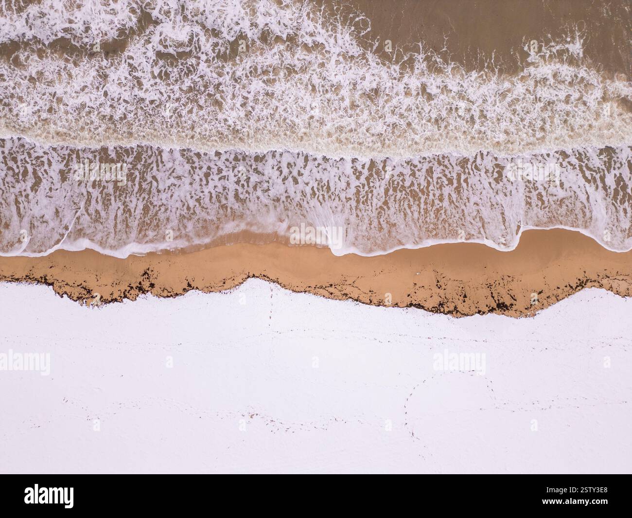 An overhead perspective of a winter shoreline where foamy ocean waves ...