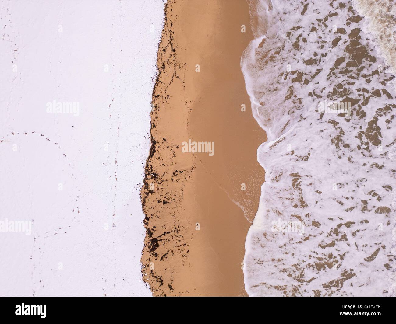 An overhead perspective of a winter shoreline where foamy ocean waves ...