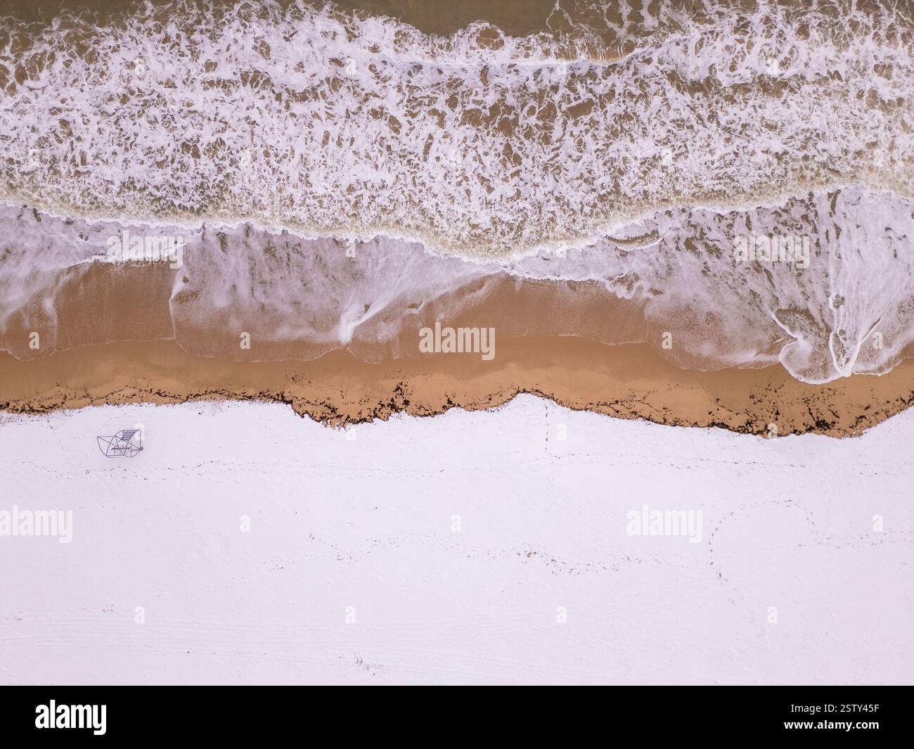 An overhead perspective of a winter shoreline where foamy ocean waves ...