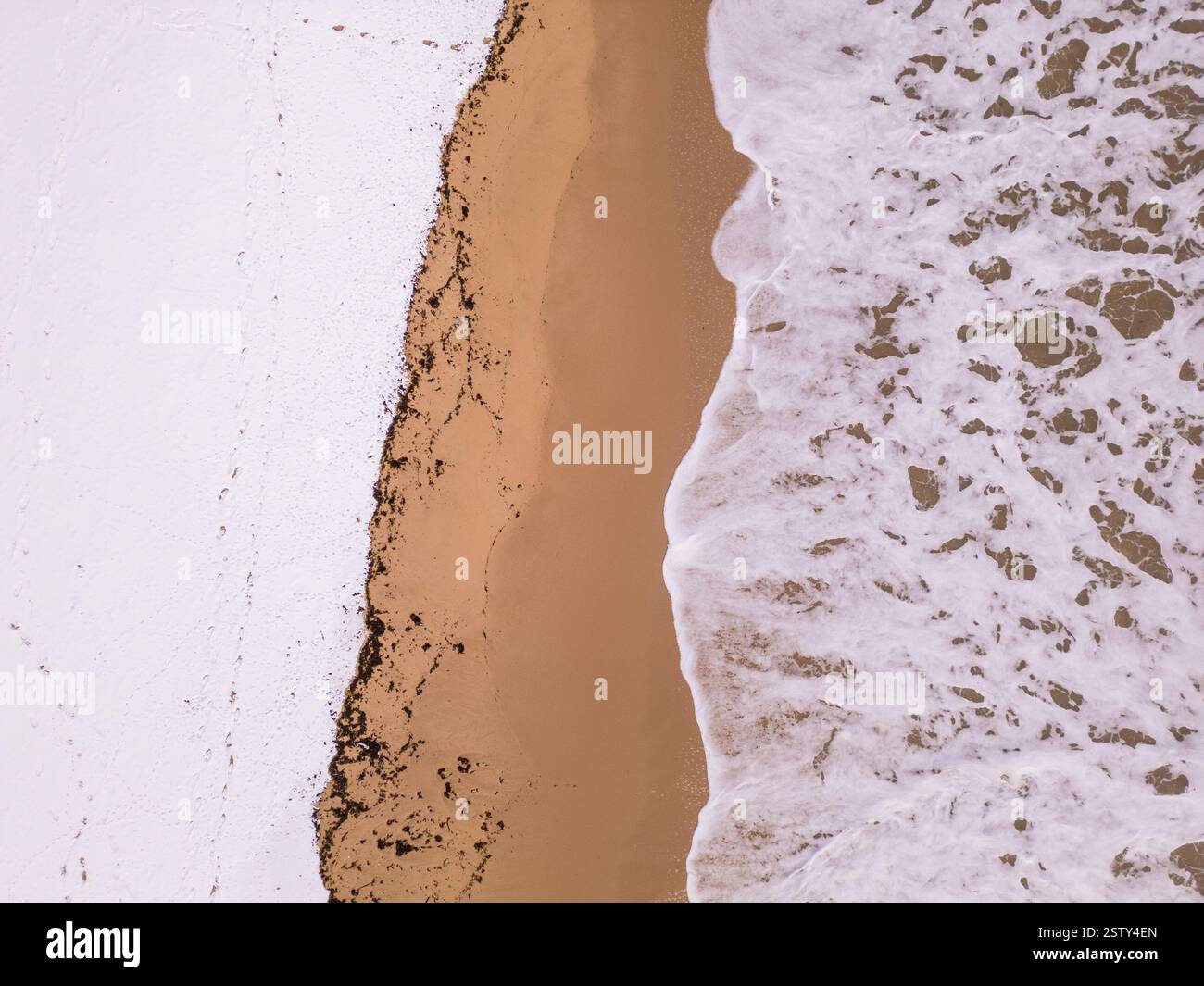 An overhead perspective of a winter shoreline where foamy ocean waves ...