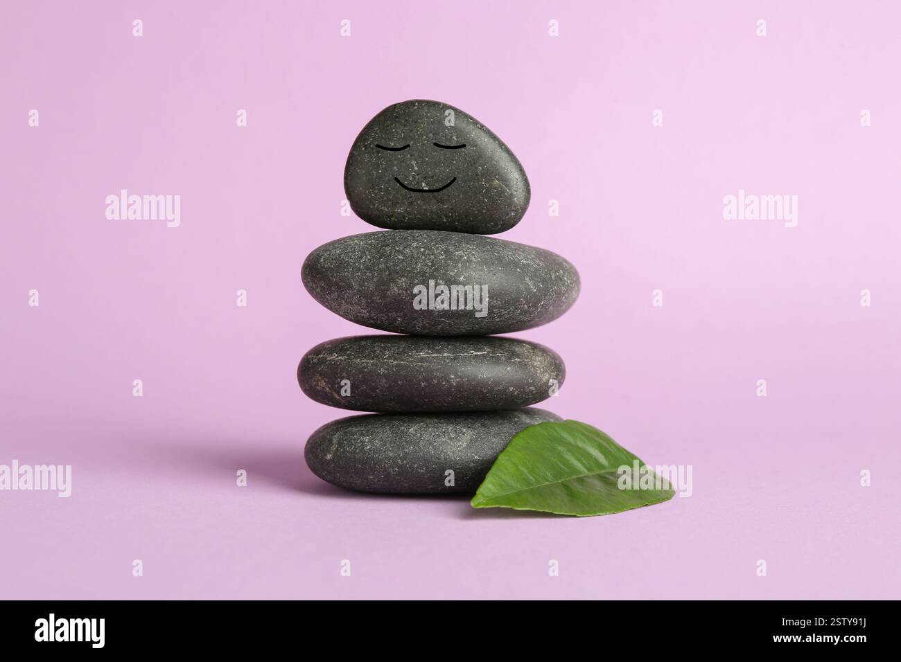 Stack of rocks with drawn smiley face on lilac background. Harmony and ...
