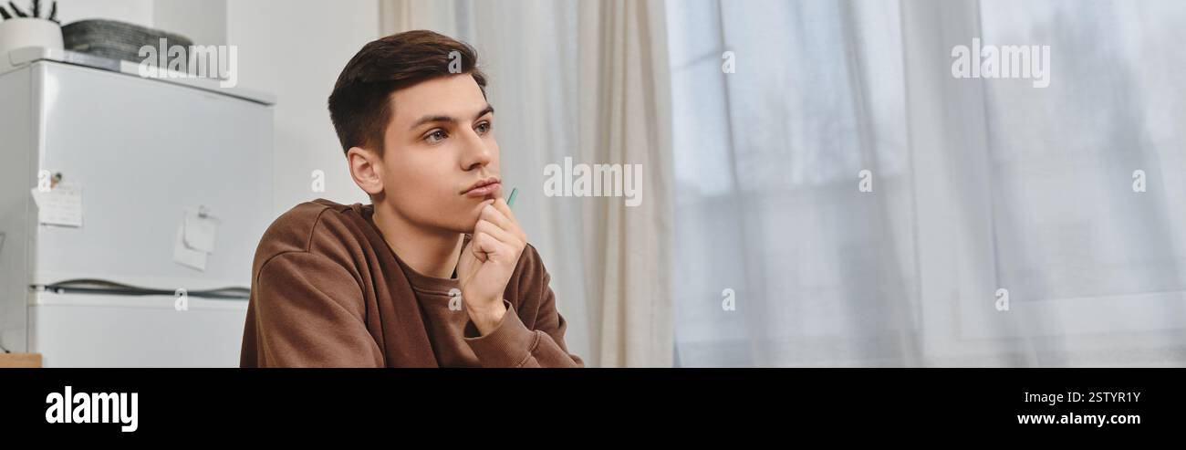 A young man reflects quietly, immersed in thoughts within a cozy home ...