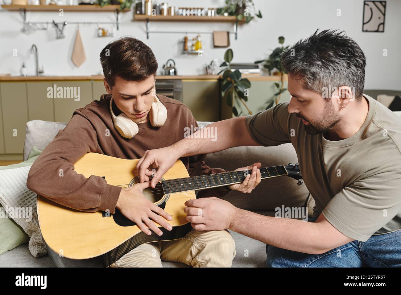 Two brothers share a warm moment as one teaches guitar skills in a cozy ...
