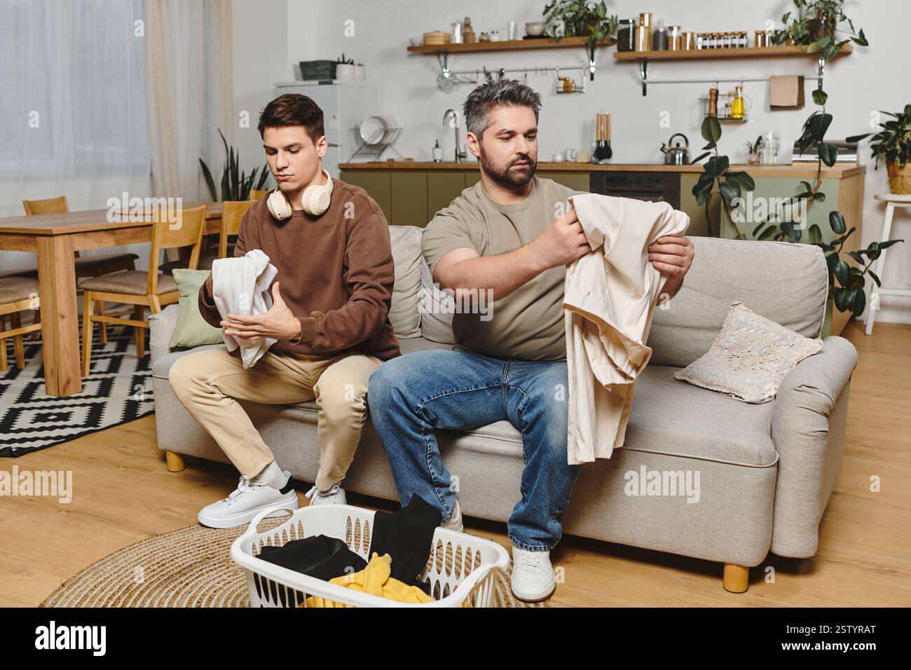 Two brothers fold laundry together on a cozy sofa, enjoying each others ...