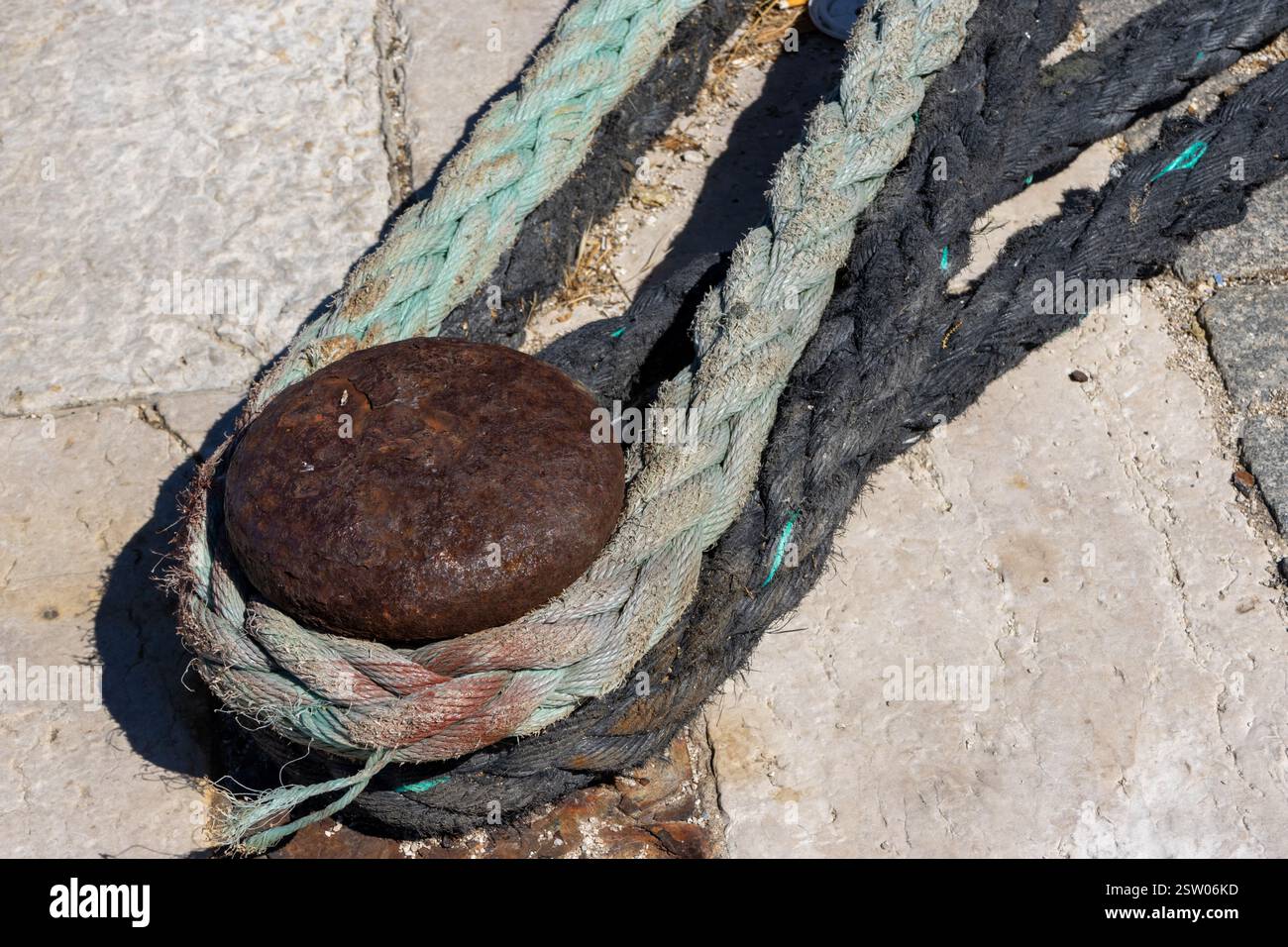 Thick ropes tied around a rusty mooring bollard on a stone dock ...