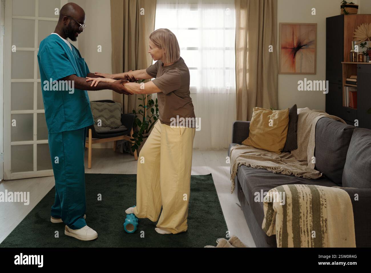 Nurse assisting elderly patient with physical exercises in cozy living ...