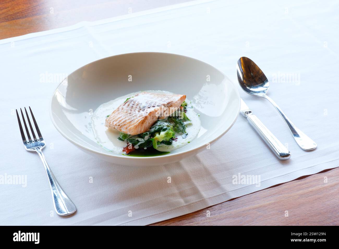 Pan seared fish fillet served with a creamy sauce and sauteed greens ...