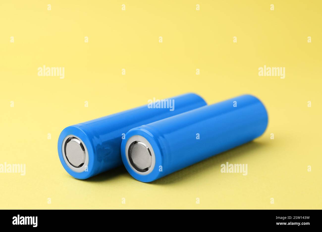 Two AA cell batteries on yellow background, closeup. Space for text ...