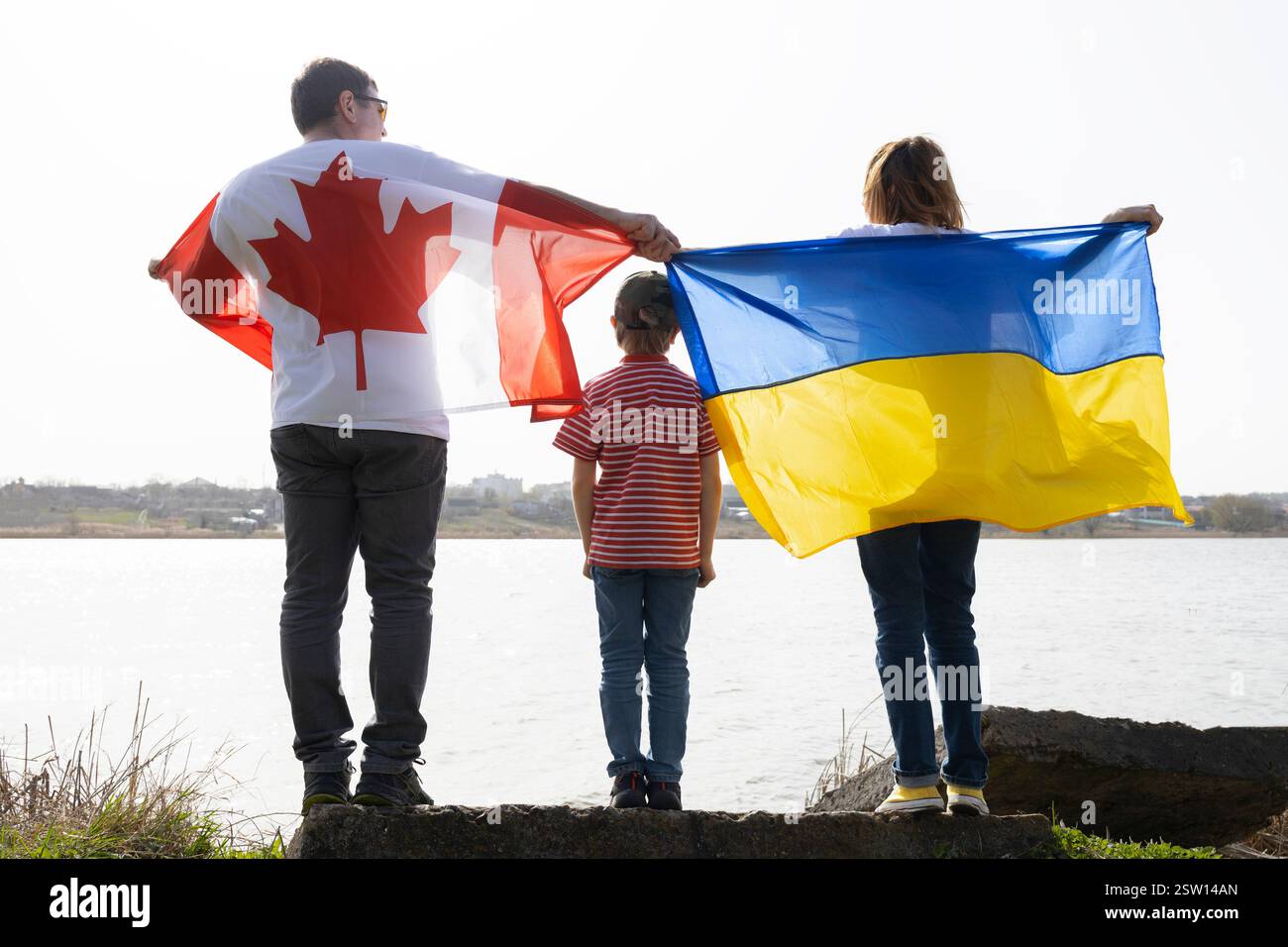father and mother with child with Ukrainian and Canadian flags standing ...
