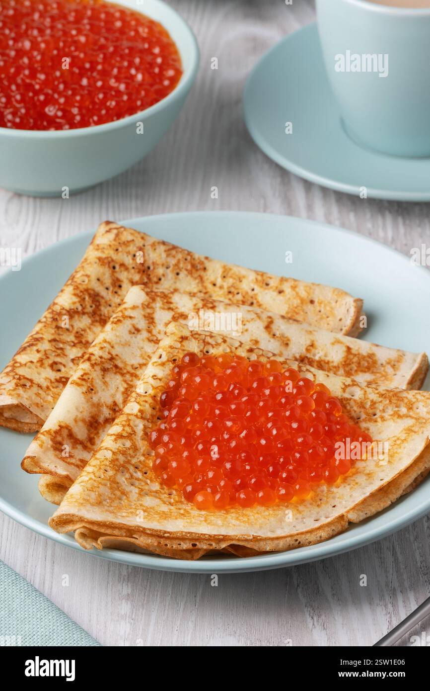 Savory crepes filled with fresh orange fish roe served on a light blue ...