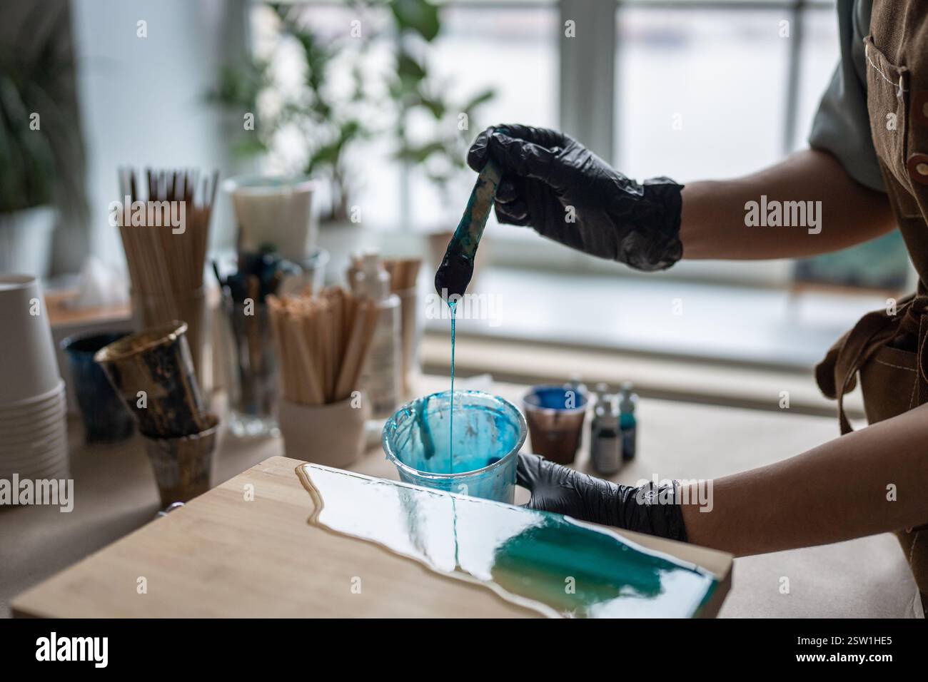 Woman artist pours epoxy resin and smears it with stick on wooden board ...