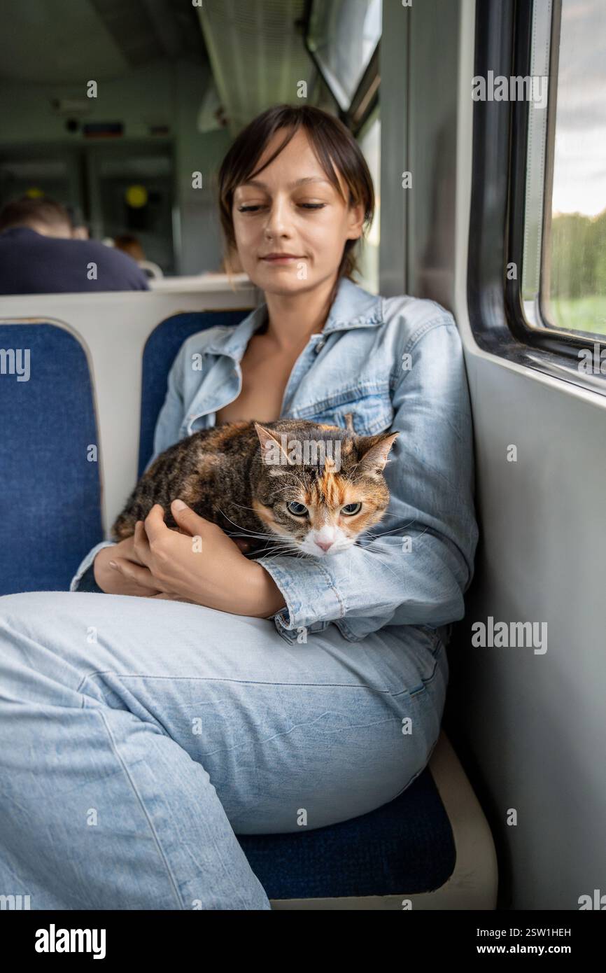 Pensive woman hugging cuddling with cat traveling in train. Stressed kitty sitting on laps of ...
