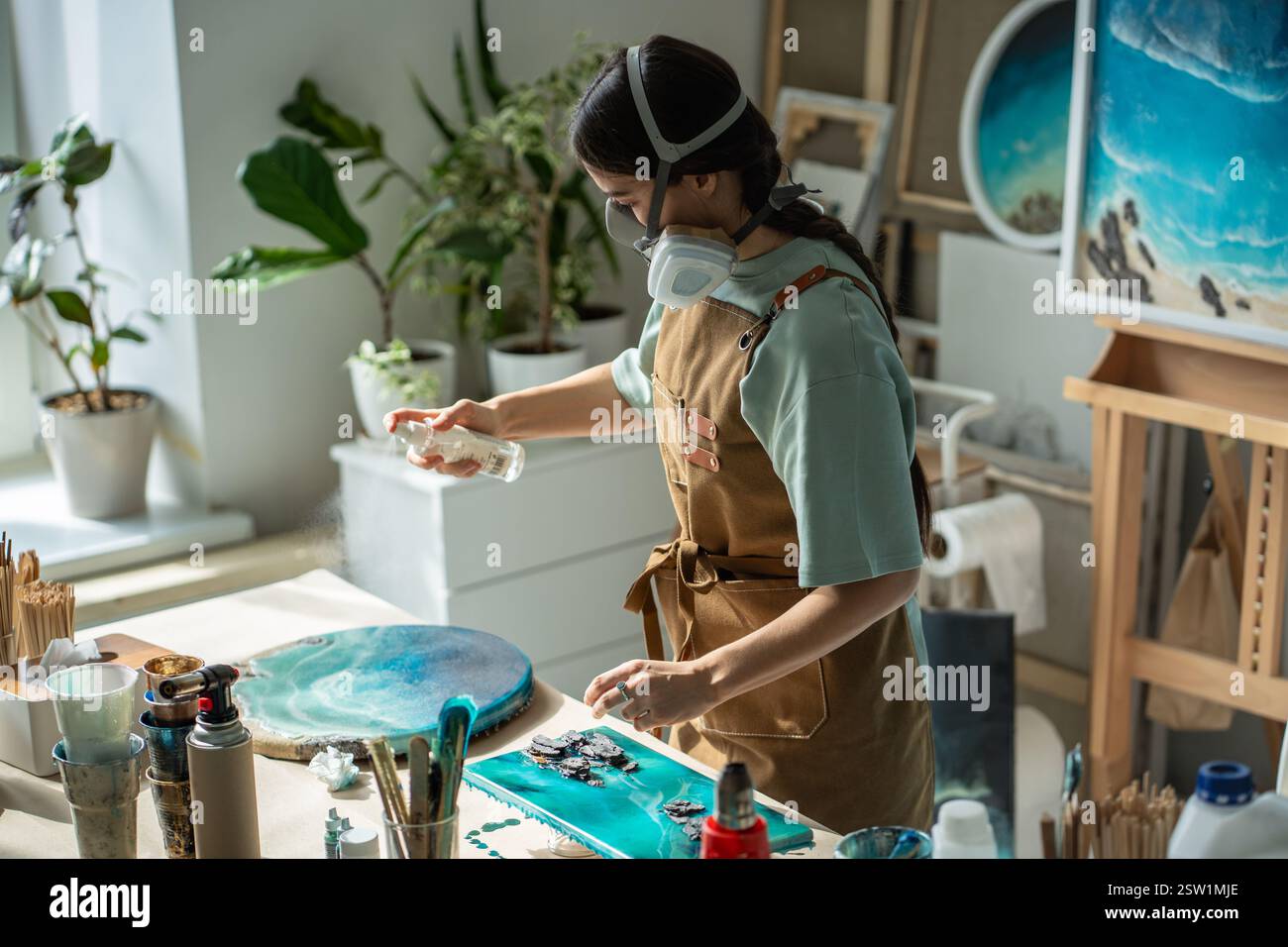 Creative artist works on epoxy resin painting, holds bottle with ...