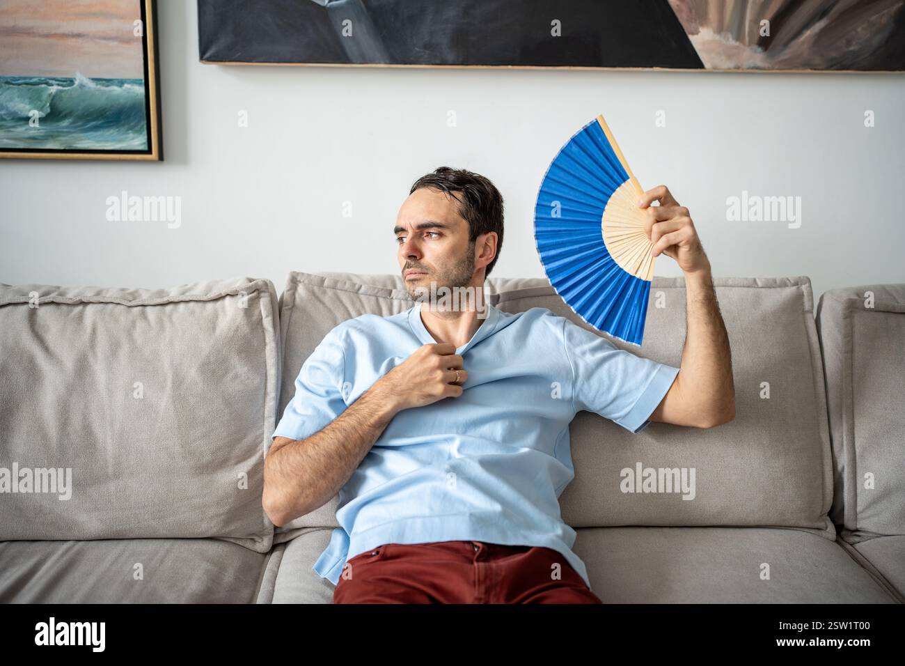 Sad man suffering from heat in apartment, fanning himself with paper ...