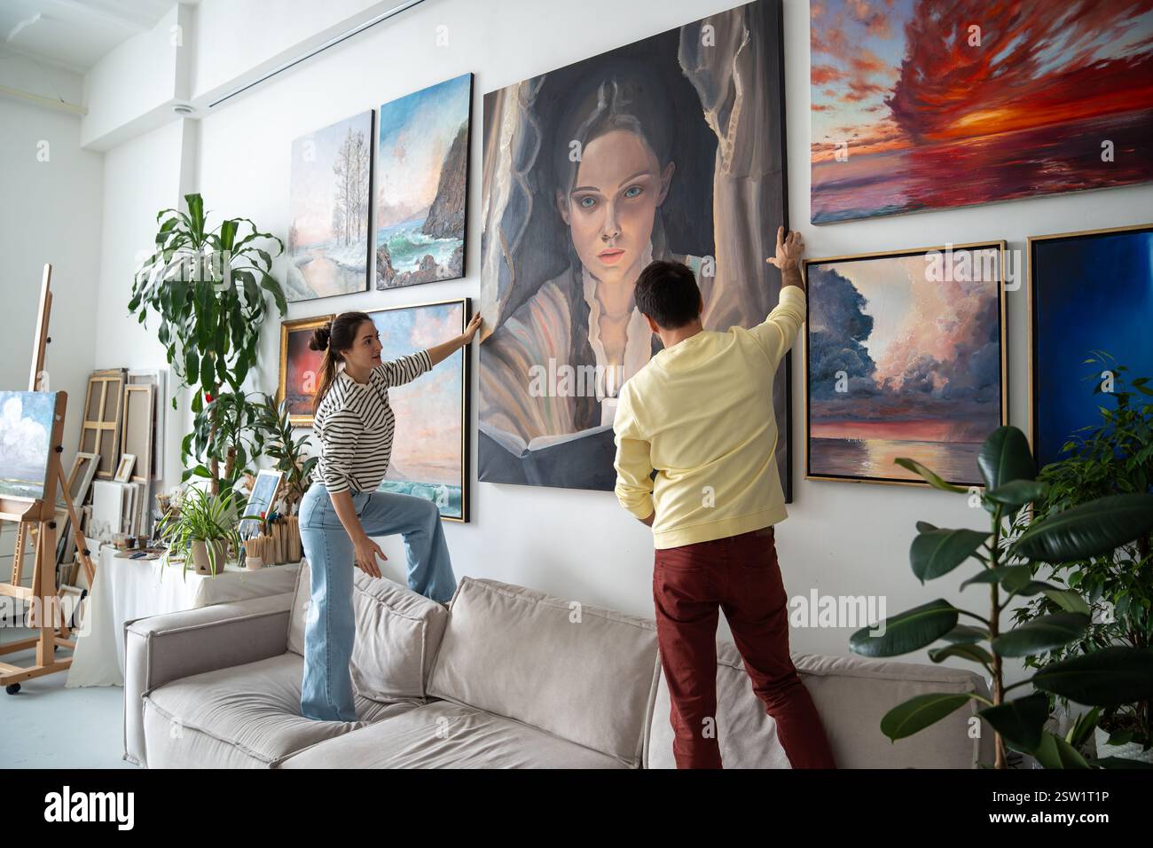 Focused interested couple of artists hang painting on wall of art ...