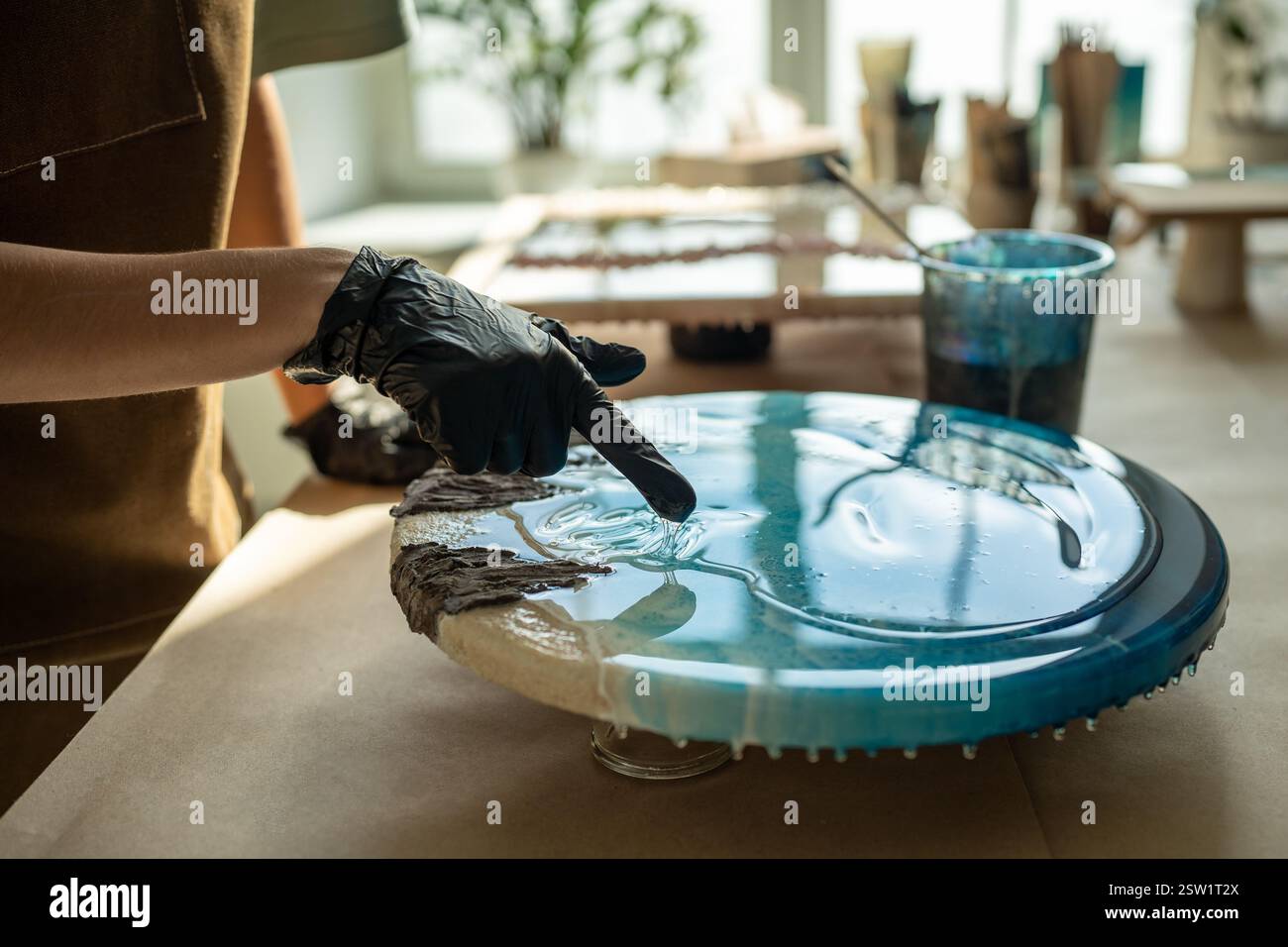 Closeup of female artist applying epoxy resin with gloved fingers in art studio closeup. Fluid ...