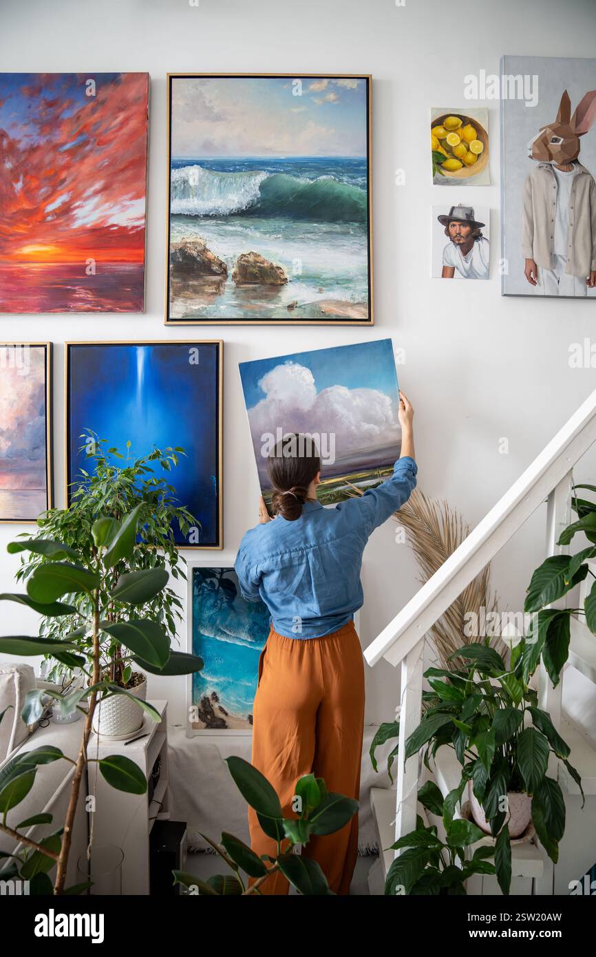 Creative woman artist hangs finished modern painting on wall in home ...