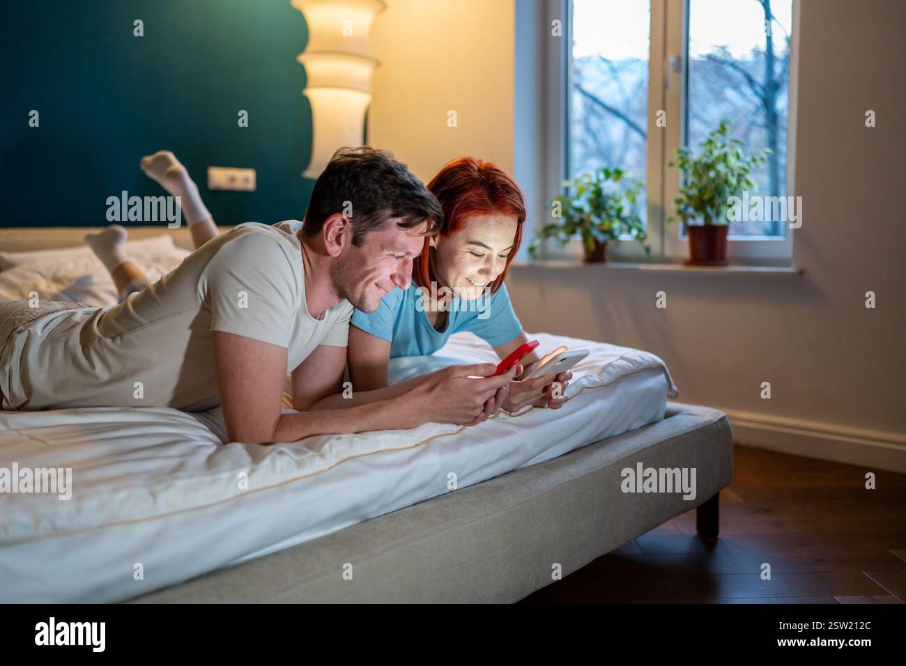Happy couple wife husband in bed looking in smartphone, smiling, talking lying in bed Stock ...