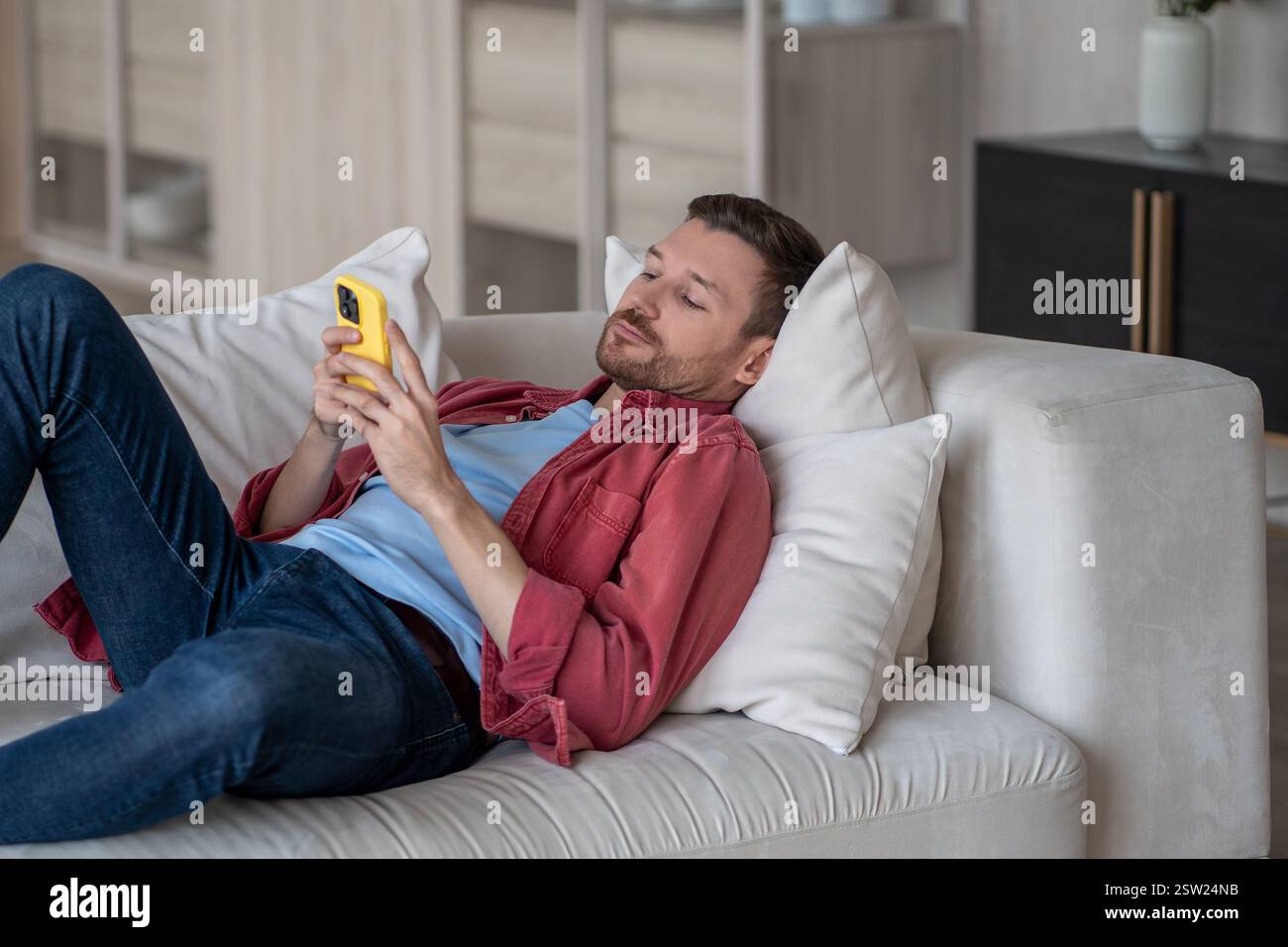 Procrastination with phone. Lazy man with social media addiction lying on couch at home scroll ...