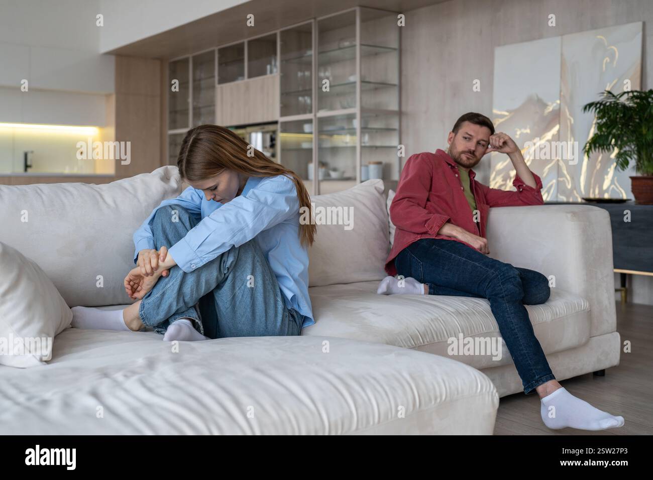 Irritated man looks at woman turned back, crying. Serious guy waits ...