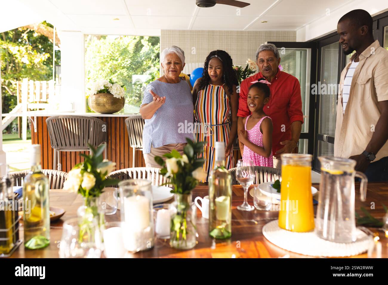 Gathering around table, multigenerational multiracial family smiling ...
