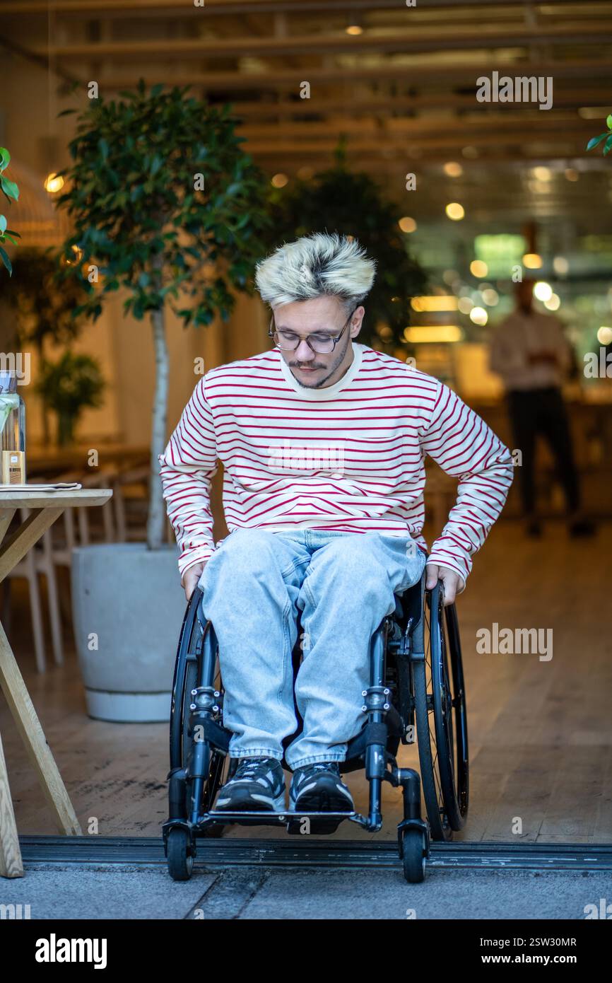 Serious focused man with disability in wheelchair drives out of cafe ...