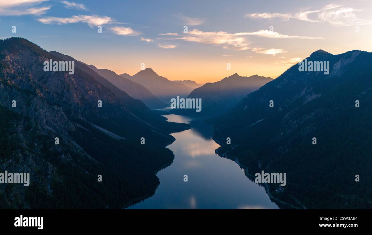 As the sun sets, the tranquil waters of Plansee mirror the surrounding ...