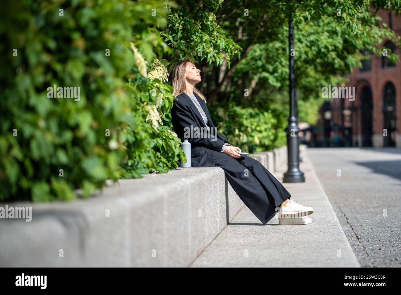 Relaxed businesswoman rest on break outside sits on concrete fence near ...