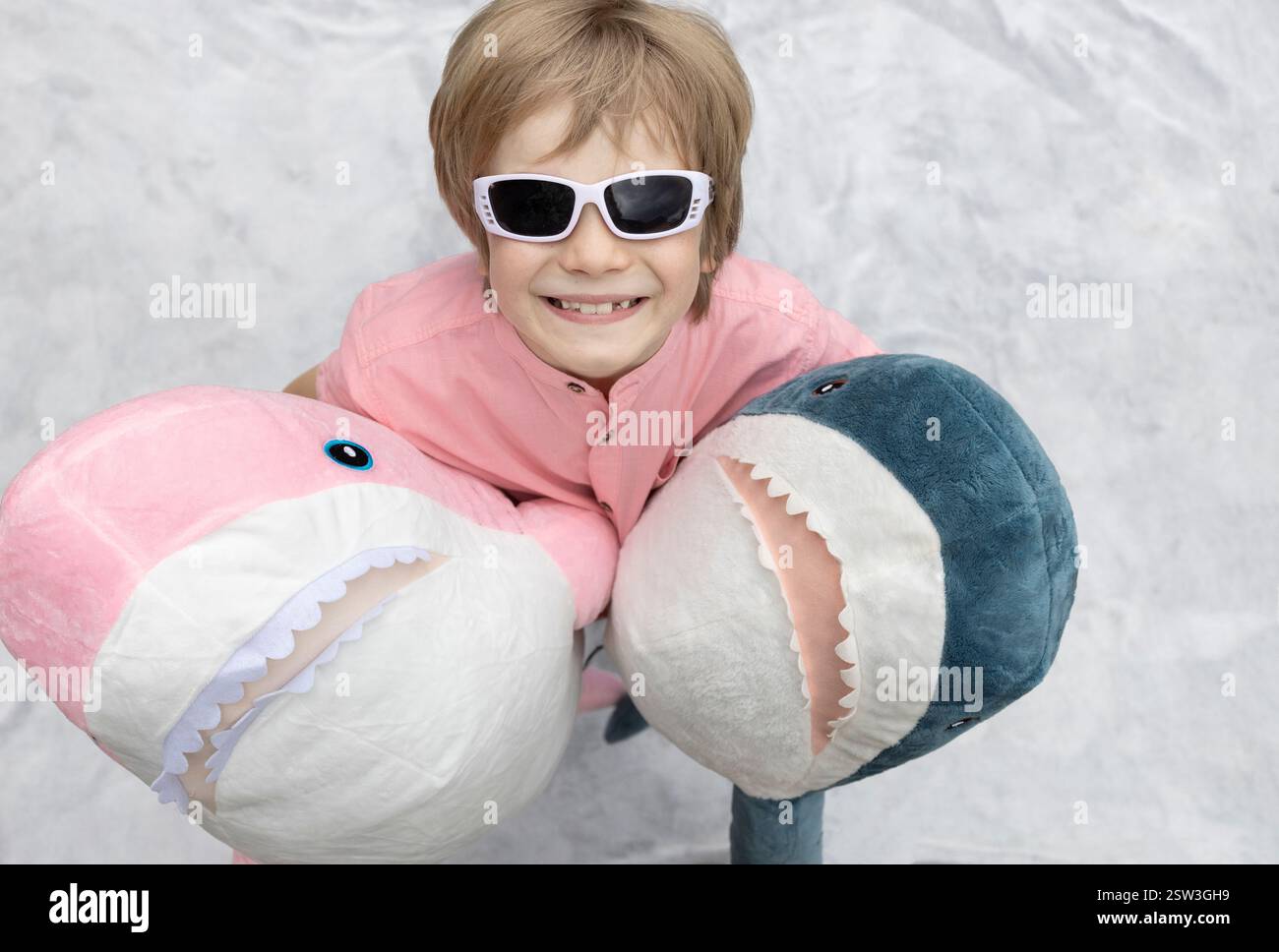 Cute face of happy boy with two big plush sharks, holds them in two ...