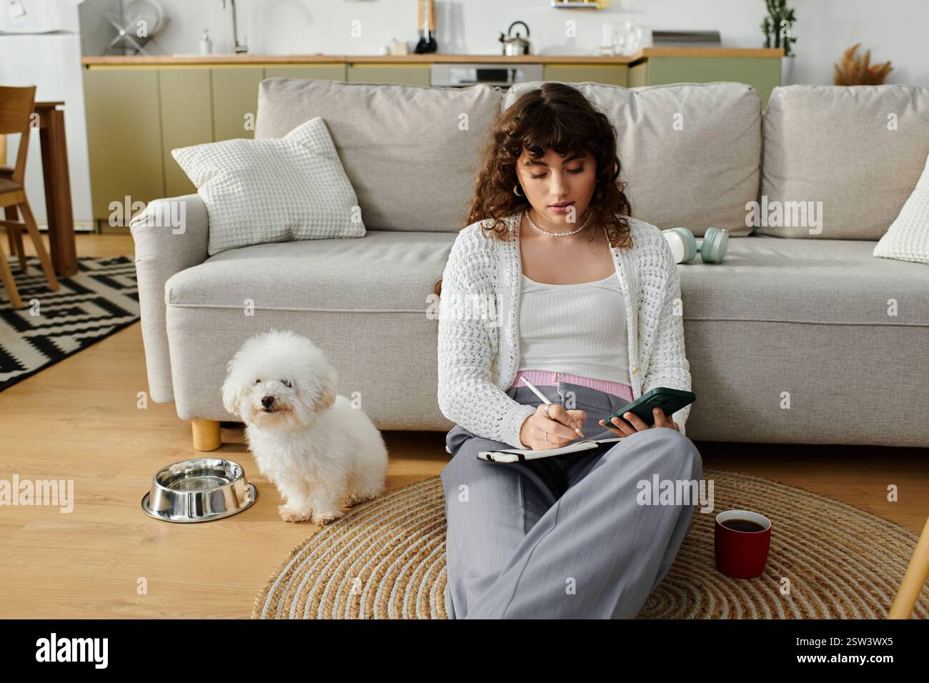 A young woman sits on the floor, writing in her notebook with her ...