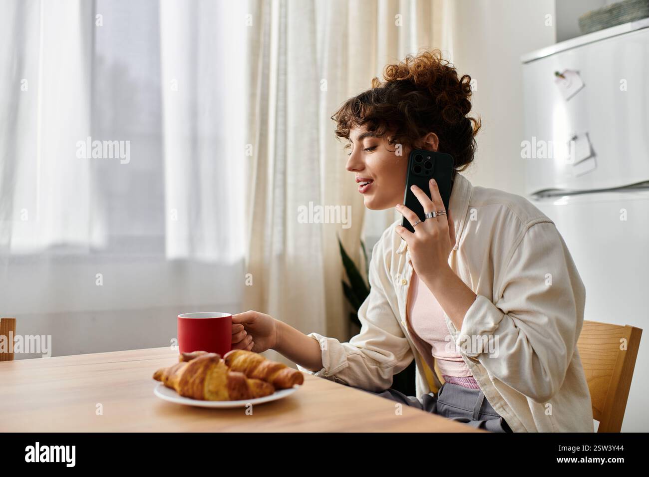 A young woman sips coffee and talks on the phone while enjoying fresh ...