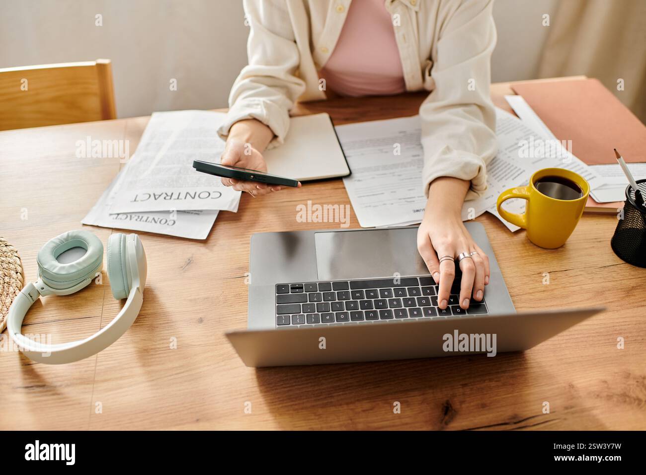 A young woman multitasks at her desk with a laptop, phone, and coffee ...