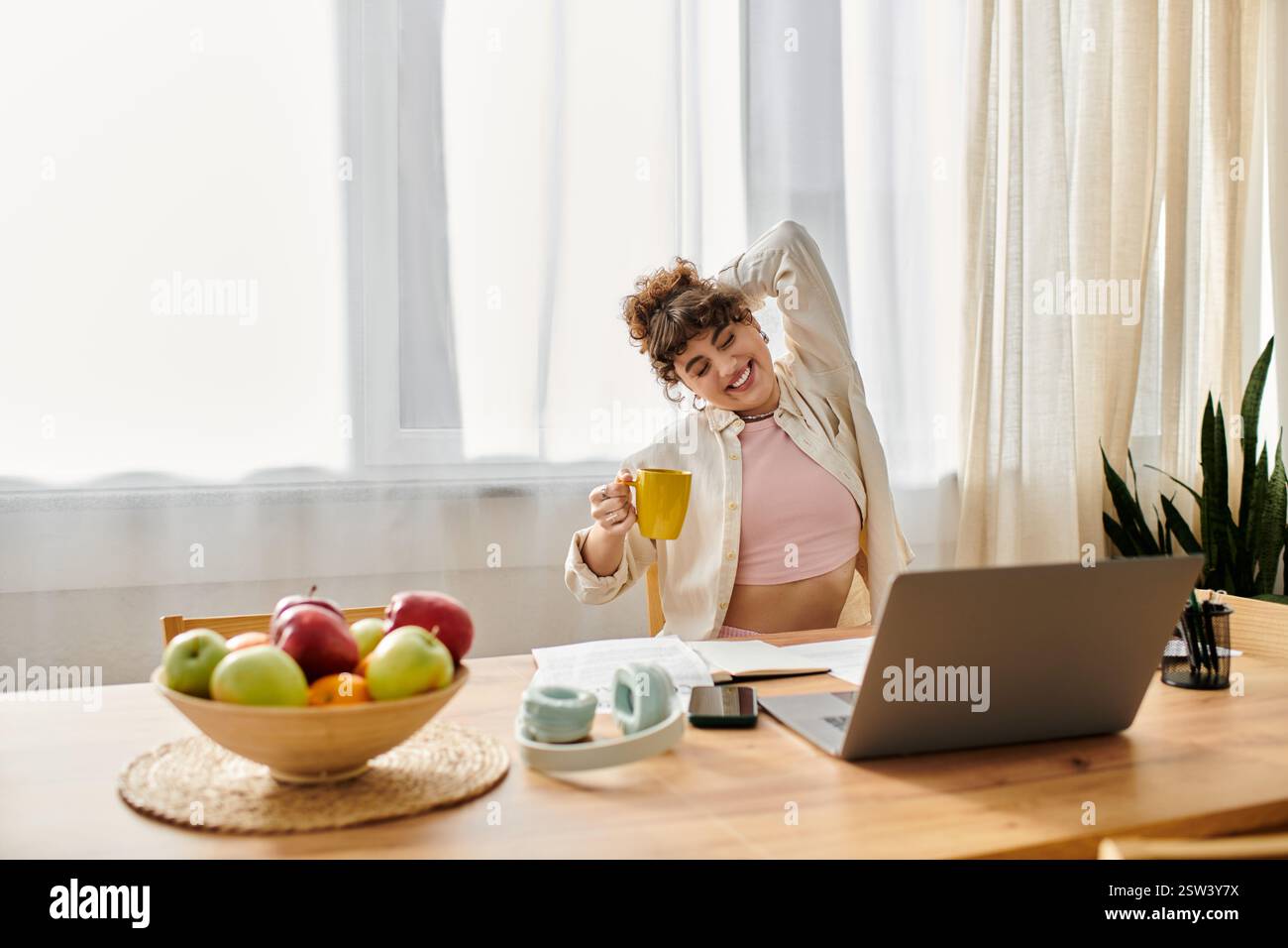 Relaxed young woman stretches while sipping tea at her cozy breakfast ...